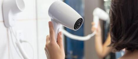 Uma pessoa usando um secador de cabelo branco num banheiro com espelho.