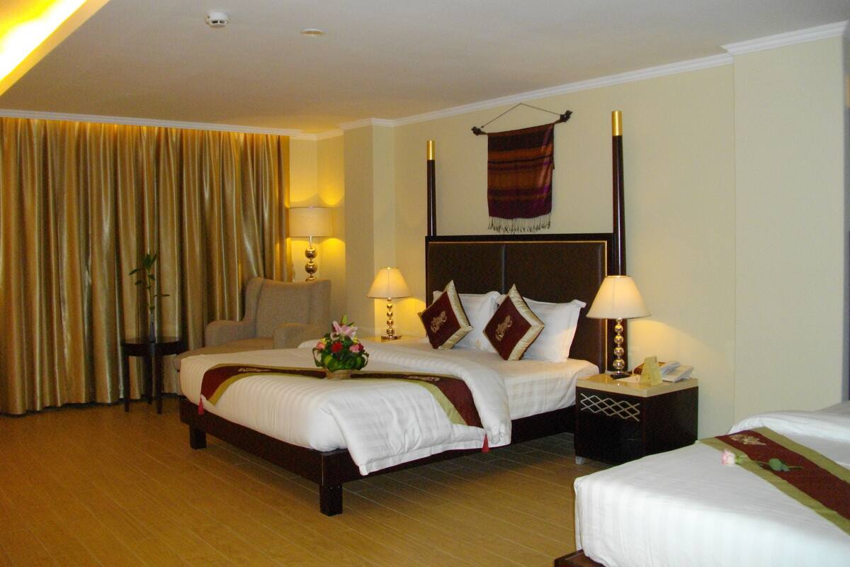 Quarto de hotel com duas camas, uma cadeira, uma mesinha de cabeceira e uma luminária.