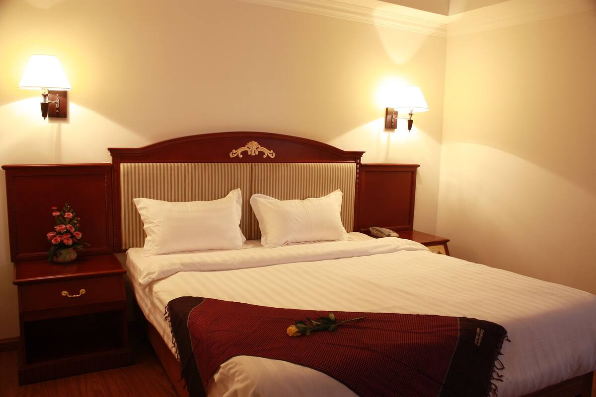Quarto de hotel com uma cama grande, duas mesas de cabeceira e uma luminária em cada lado da cama.