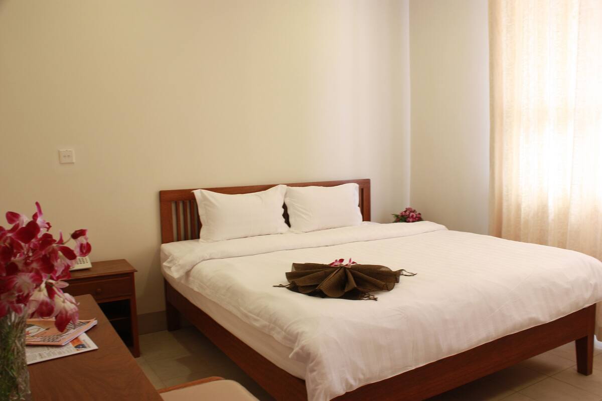 Cama bem arrumada com lençóis brancos, cabeceira de madeira e um laço decorativo na cama.
