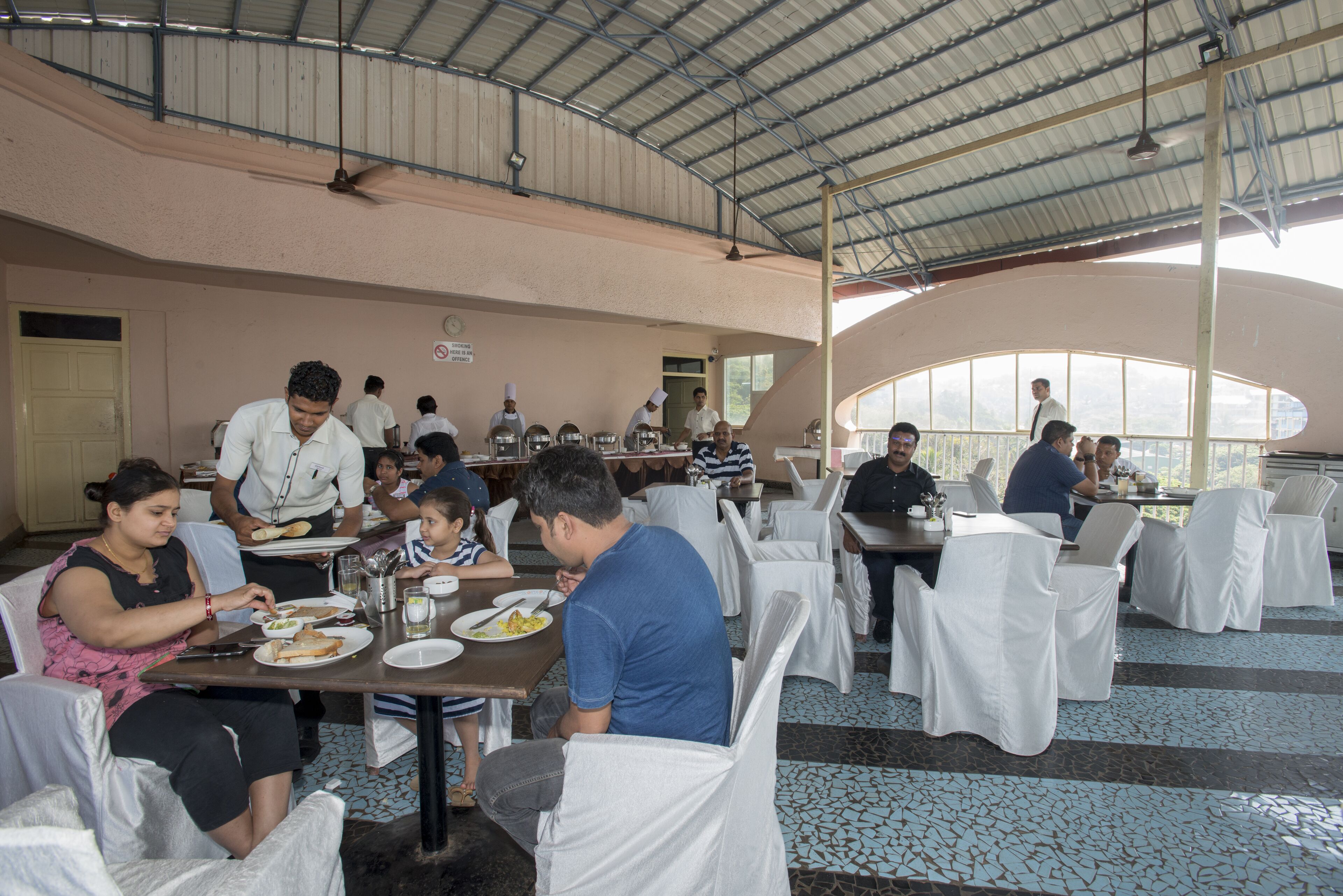 Um restaurante com mesas cobertas por toalhas brancas, chão de azulejos e teto alto com vigas de metal.