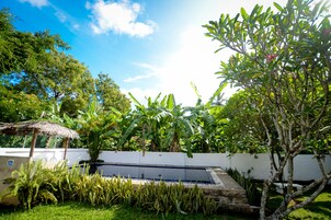 Um jardim com piscina, vegetação exuberante e uma construção de telhado de palha.