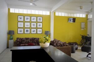 Uma sala de estar com parede amarela, um sofá, uma mesa de centro com um vaso de flores e uma televisão fixada na parede.