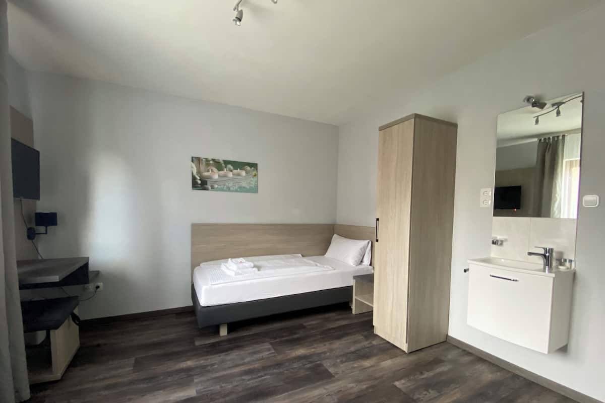 Quarto com cama, guarda-roupa de madeira, mesa de cabeceira, espelho e televisão na parede.