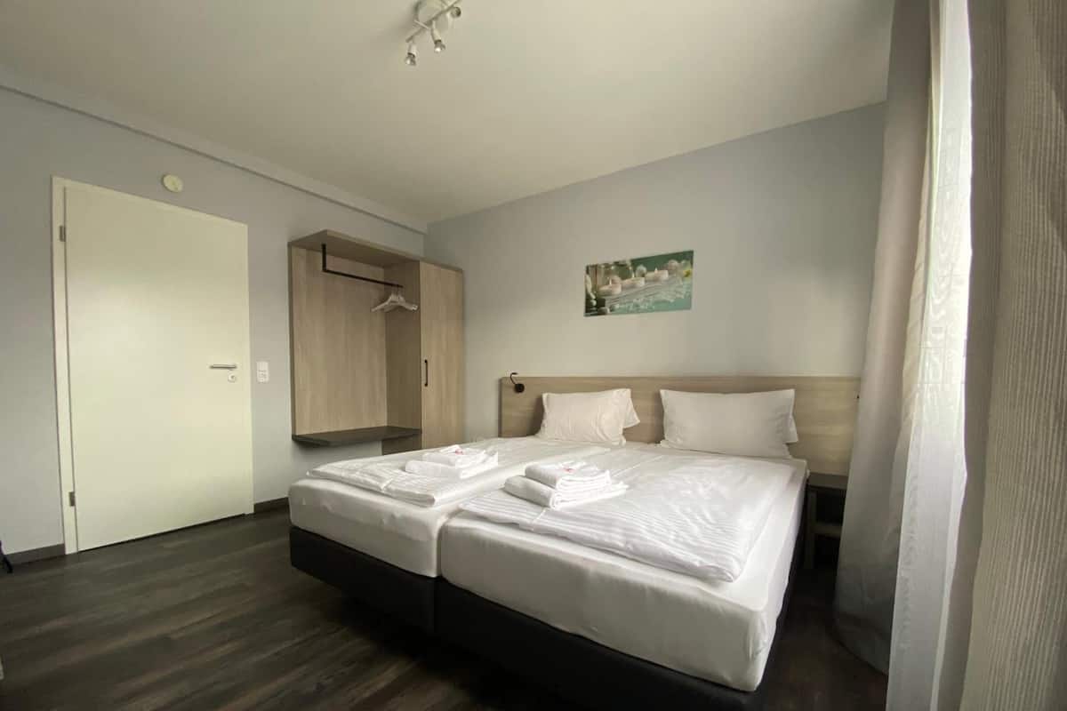 Quarto de hotel com uma cama de casal, um guarda-roupa, um quadro na parede e uma porta.