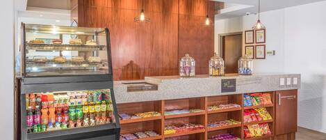Um bar de petiscos com diversos alimentos e bebidas, incluindo um balcão refrigerado e prateleiras cheias de lanches.