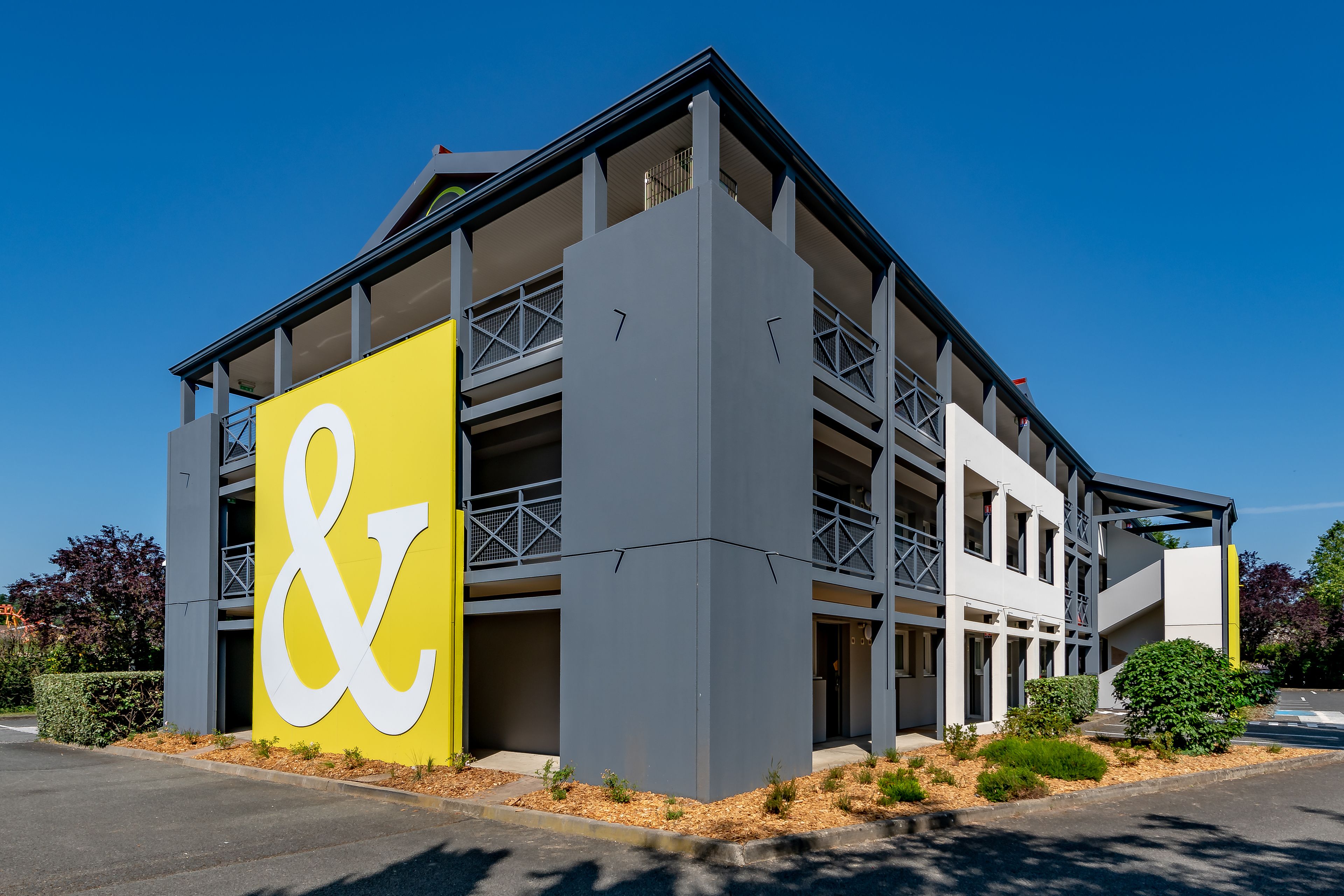 Um edifício moderno com uma placa amarela e branca em destaque, várias varandas e fachada estruturada.
