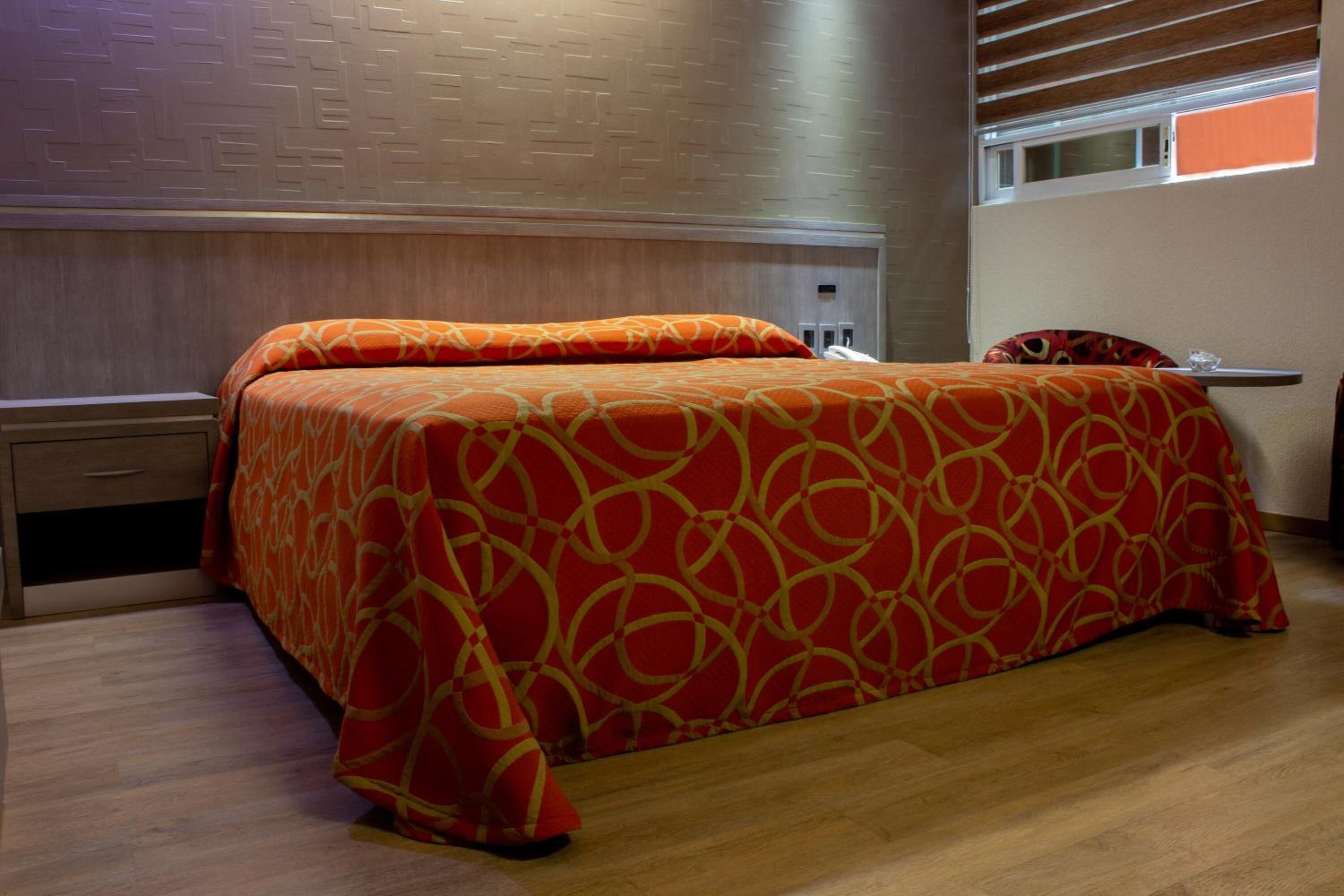 Quarto de hotel com cama, mesa de cabeceira e janela.