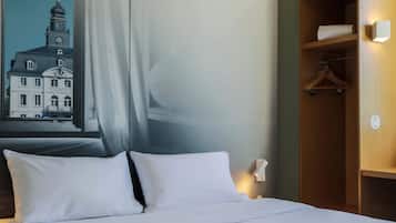 Quarto de hotel com uma cama, um guarda-roupa e um quadro de um edifício.