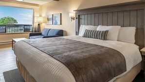 Quarto com cama grande, mesa de cabeceira, luminária, sofá e vista para o exterior.