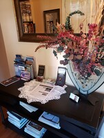 Bancada de recepção com folhetos informativos, uma placa emoldurada e um arranjo decorativo de plantas.
