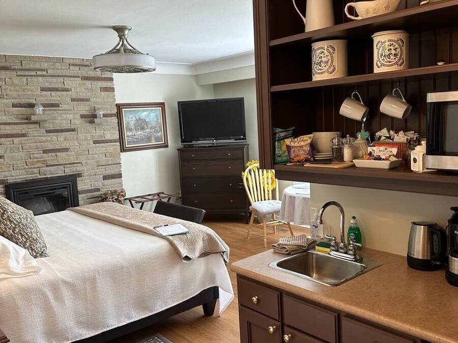 Quarto com cama, cômoda, televisão e área de cozinha com pia e armários.