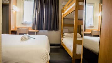 Quarto de hotel com beliche, escrivaninha, cadeira e janela com cortinas.