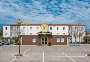 Um hotel tipo bed and breakfast com fachada amarela e marrom, um estacionamento e um céu azul límpido.