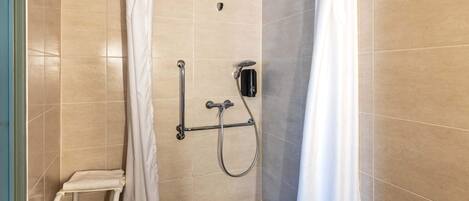 Pequeno espaço de chuveiro revestido com azulejos, com cortina branca, chuveiro manual e um banquinho.