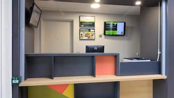 Uma área de recepção com balcão, computador e tela na parede.