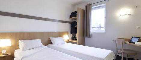 Quarto de hotel com duas camas, uma escrivaninha, um laptop, uma cadeira e uma janela com cortinas.