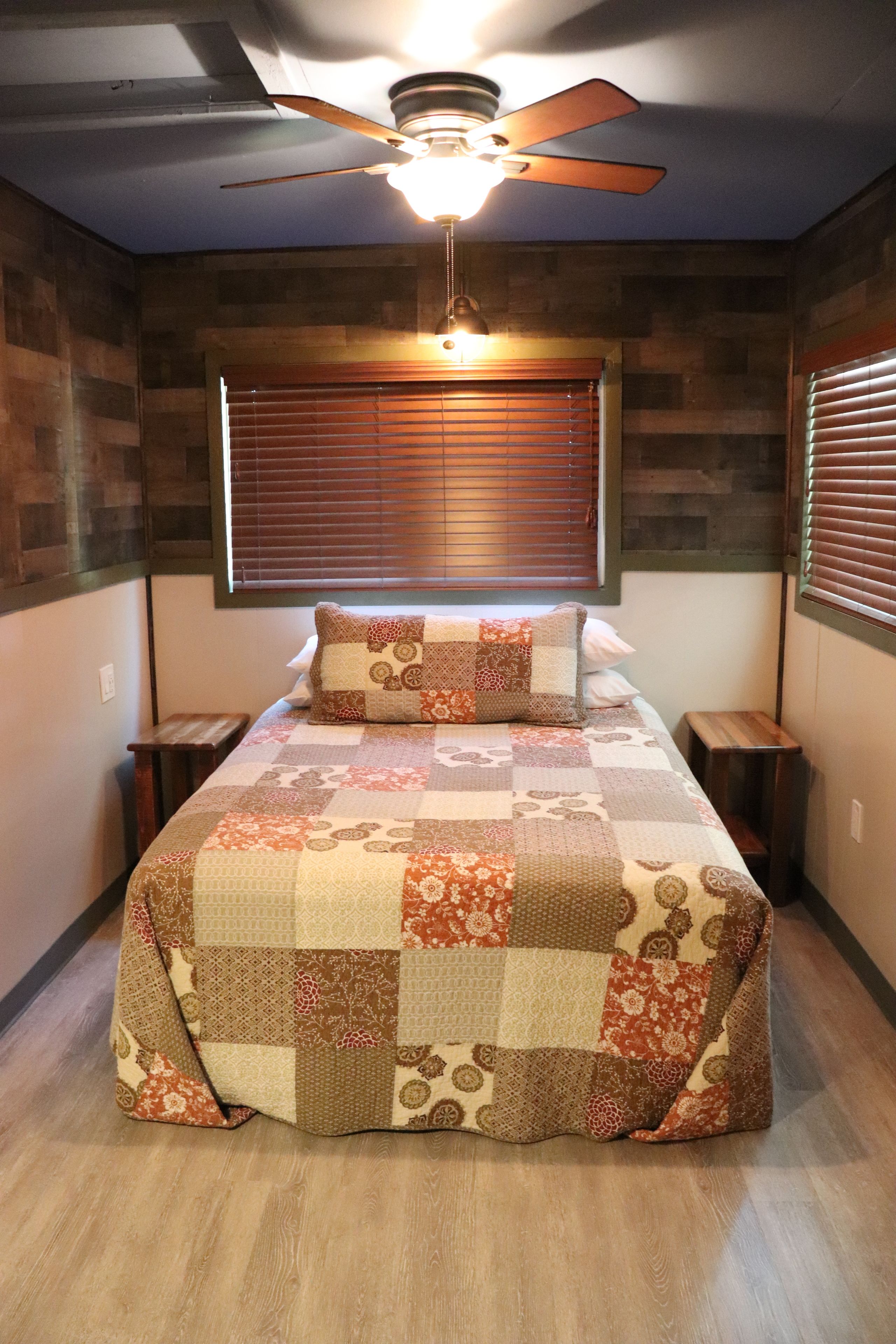 Quarto com cama grande, paredes de madeira, ventilador de teto e janela com persianas.