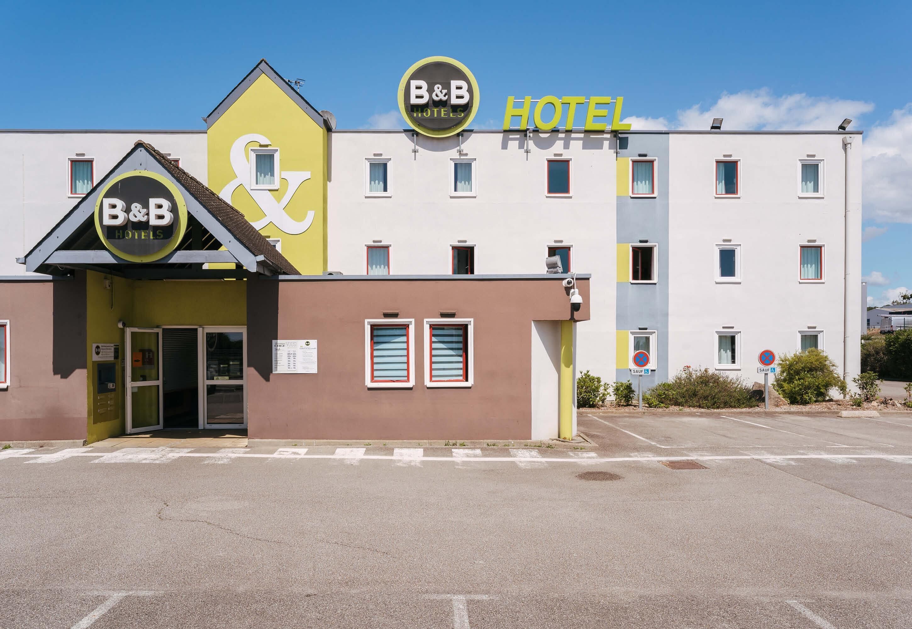 Uma pousada com fachada amarela, entrada marrom e placa indicando que é um hotel.