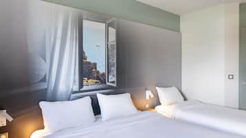 Quarto de hotel com cama, mesa de cabeceira, janela com vista para o mar e luminária na parede.