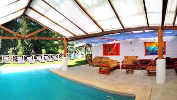 Uma área de piscina interna com terraço coberto, espreguiçadeiras e piscina.