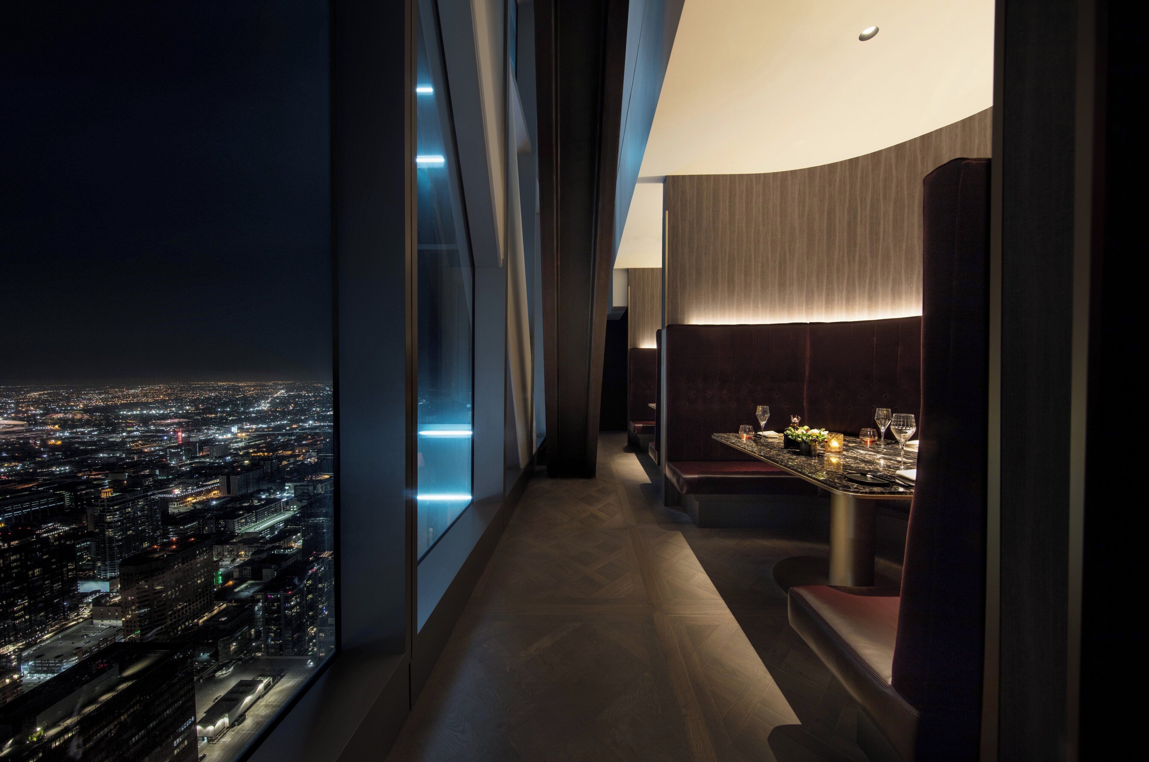 Interior moderno com vista para a cidade à noite, um corredor longo e uma área de jantar com mesa posta para dois.