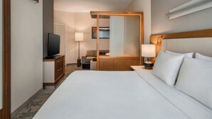 Quarto de hotel com cama, televisão, escrivaninha, abajur e espelho.