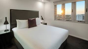 Quarto de hotel com uma cama grande, duas mesas de cabeceira com abajures, uma janela com vista para a cidade e uma luz noturna.