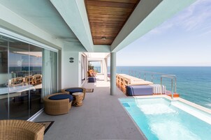 Uma varanda com piscina, mobiliário de vime e vista para o oceano.