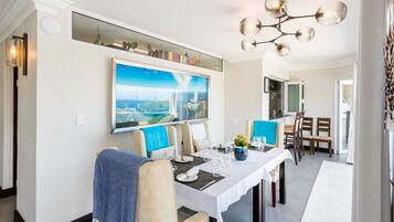 Uma sala de jantar com uma mesa posta para quatro pessoas, um quadro grande acima da mesa e um candelabro.