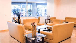 Uma área de espera moderna com poltronas de couro, uma mesa de centro de vidro e um vaso com flores.