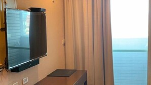 Quarto com televisão de tela plana na parede, escrivaninha de madeira e janela com cortinas.