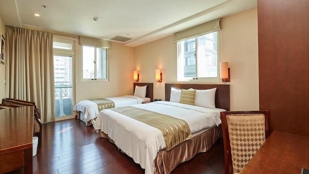 Quarto de hotel com duas camas, uma escrivaninha e um espaço para refeições.
