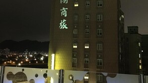 Um edifício com vários andares e sinalização iluminada em escrita estrangeira, provavelmente indicando um hotel ou propriedade comercial.