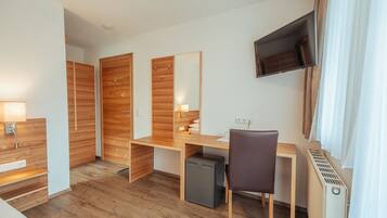 Quarto de hotel moderno com escrivaninha de madeira, uma cadeira, um frigorífico pequeno, televisão fixada na parede e janela com cortinas.