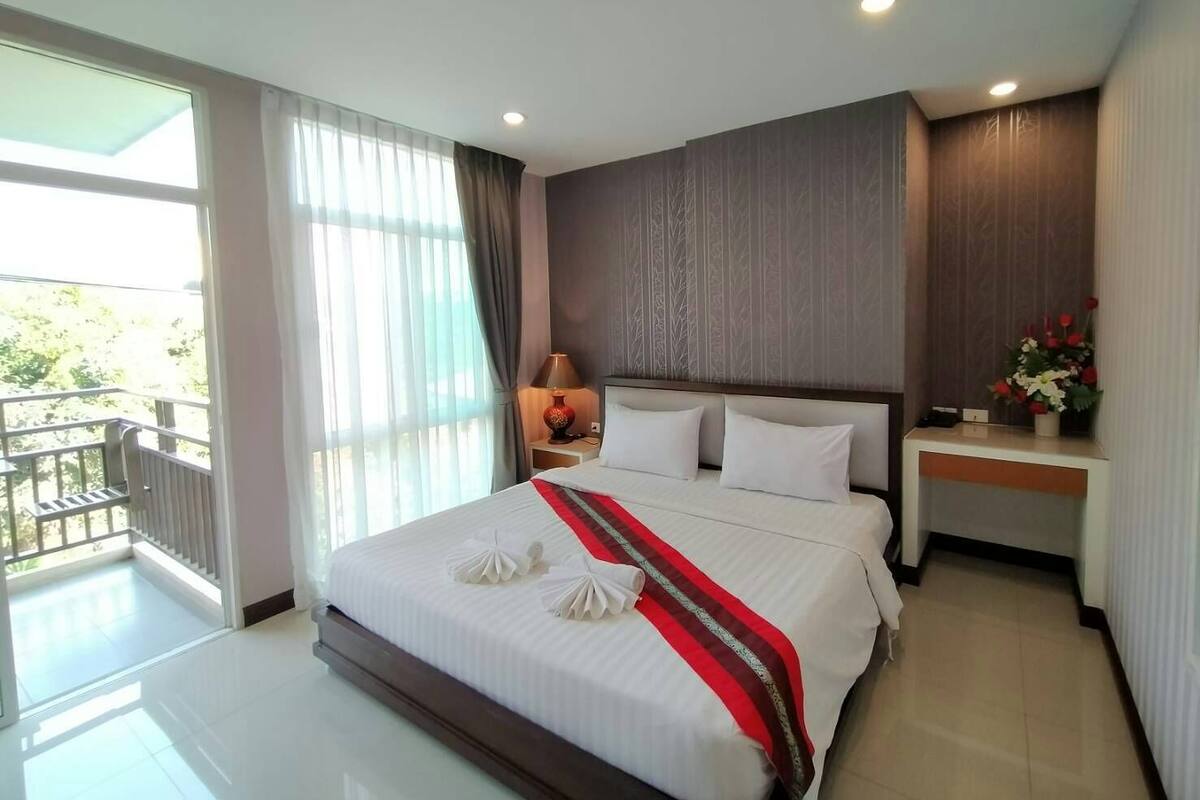 Quarto de hotel moderno com uma cama grande, mesa de cabeceira, luminária e vista para o exterior.