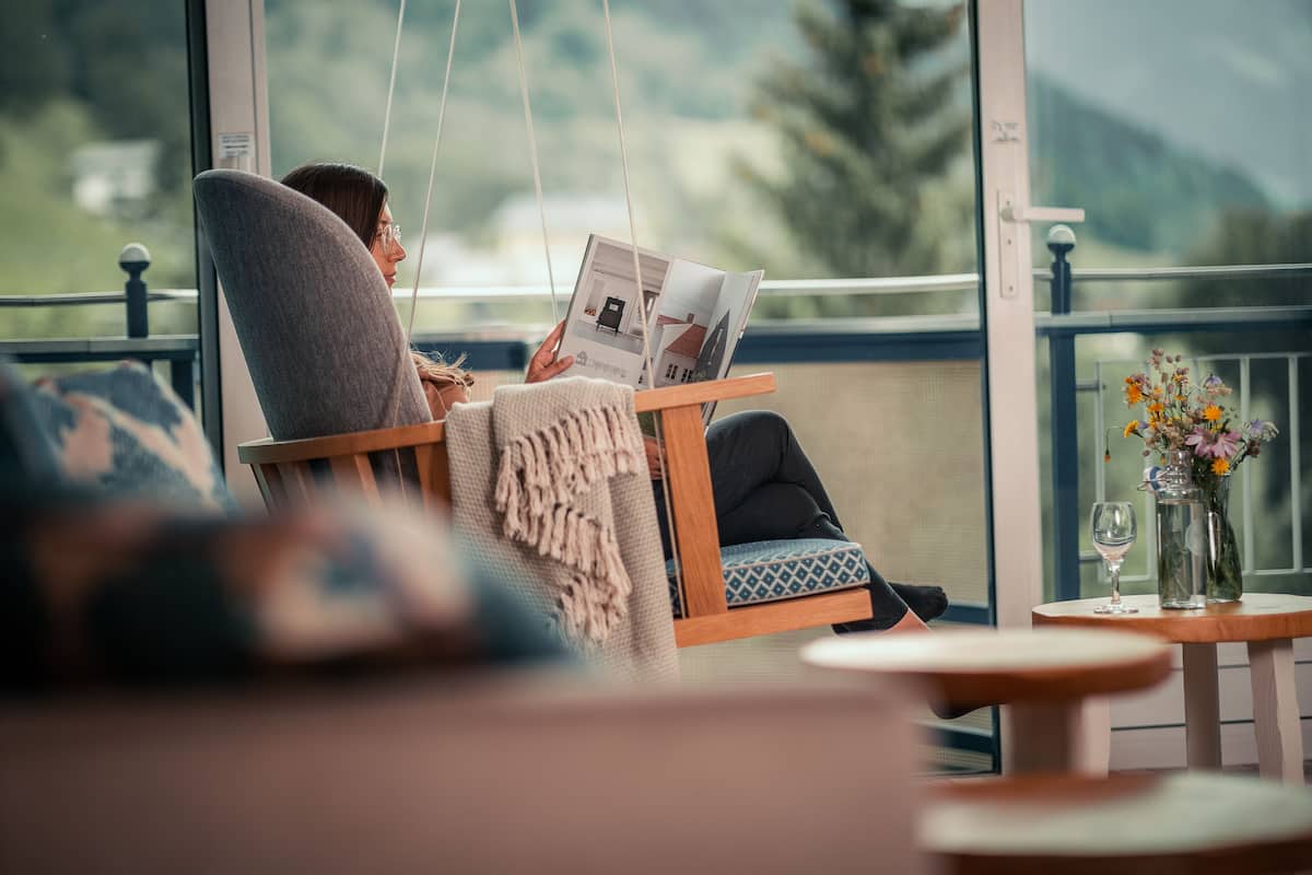 Uma pessoa lendo uma revista numa varanda com vista para montanhas.