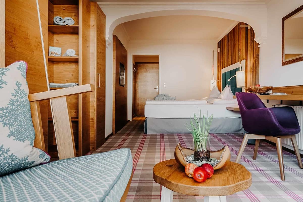 Quarto de hotel com uma cama, uma escrivaninha, uma cadeira, um sofá e uma mesinha com frutas e um vaso.