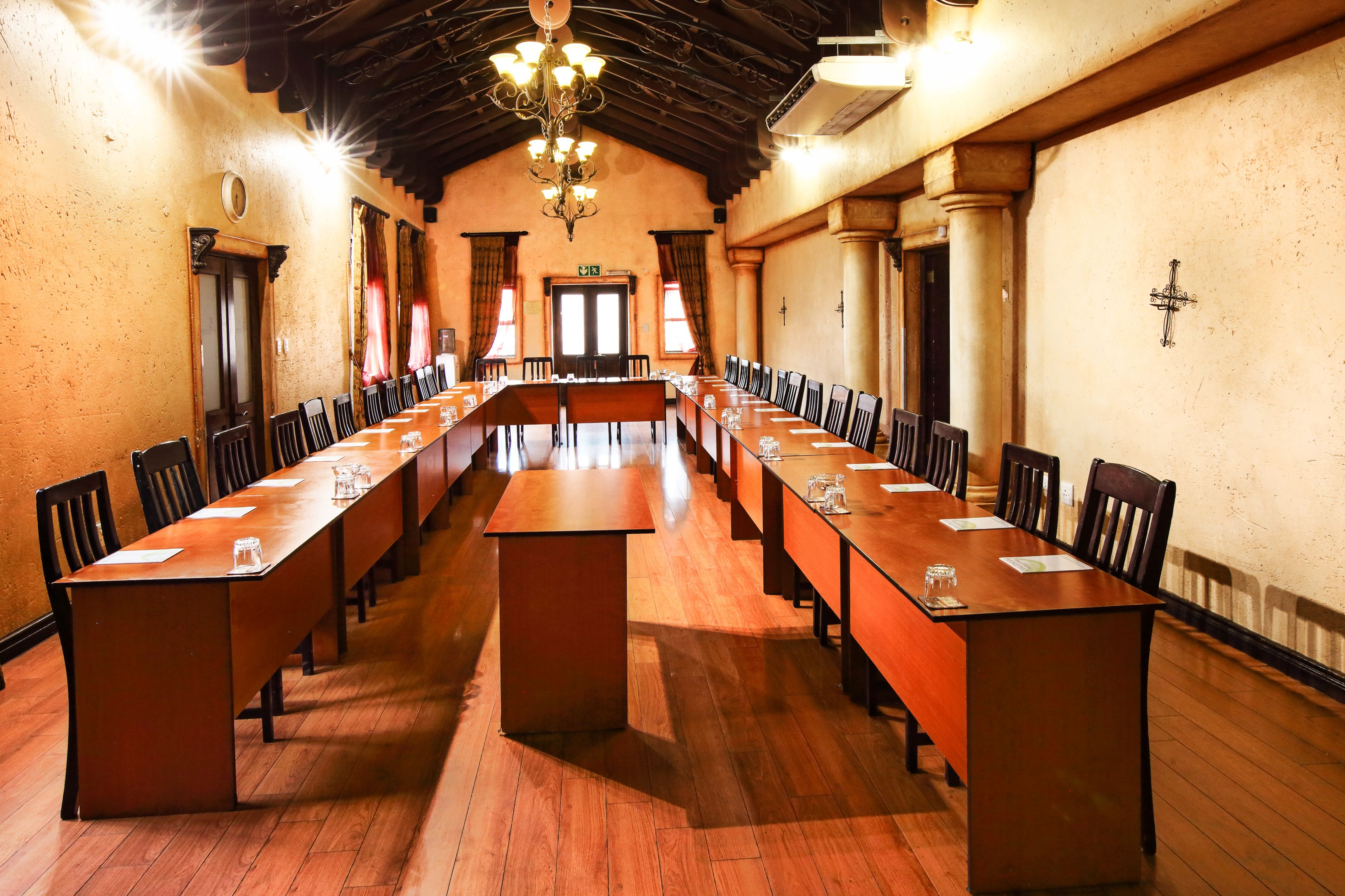 Uma sala de conferências com mesas e cadeiras compridas, piso de madeira e um lustre.