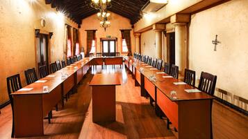 Uma sala de conferências com mesas e cadeiras compridas, piso de madeira e um lustre.