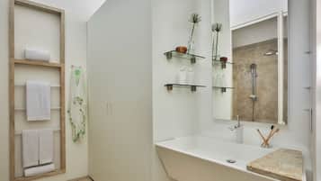 Um banheiro moderno com toucador branco, box de vidro e porta-toalhas de madeira.
