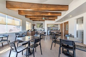 Uma área de refeições moderna com vigas de madeira, cadeiras pretas e uma ilha central com cafeteira.