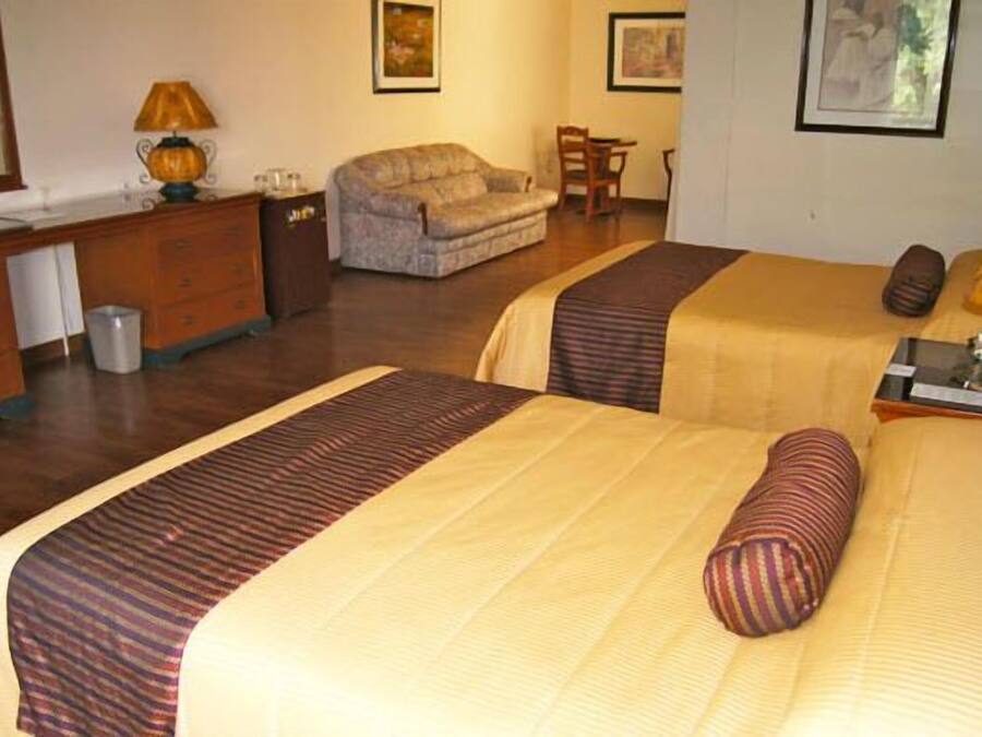 Quarto de hotel com duas camas, uma escrivaninha, uma cadeira, um sofá e uma televisão.