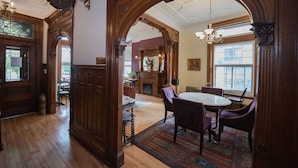 Uma elegante sala de jantar com mesa e cadeiras de madeira, um candelabro e vista para o exterior através de uma grande janela.