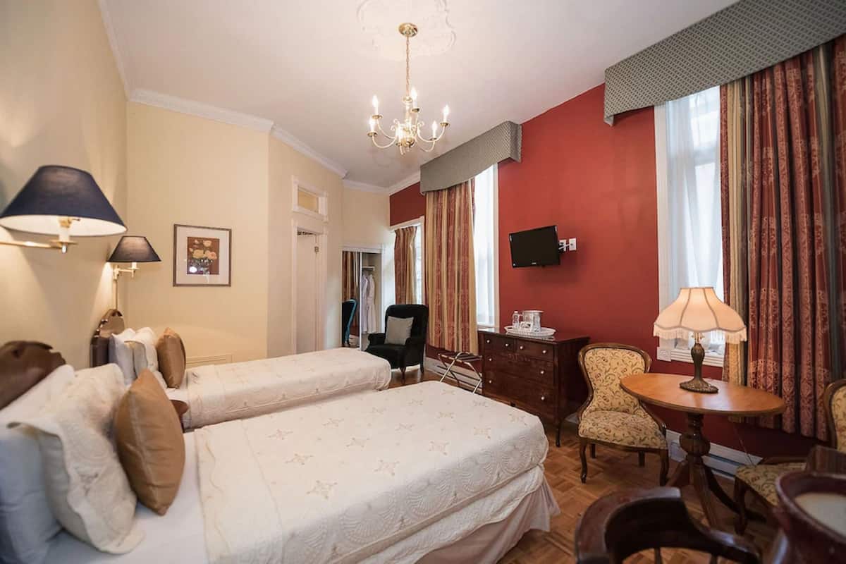 Quarto de hotel com duas camas, televisão, escrivaninha, cadeira e abajur.