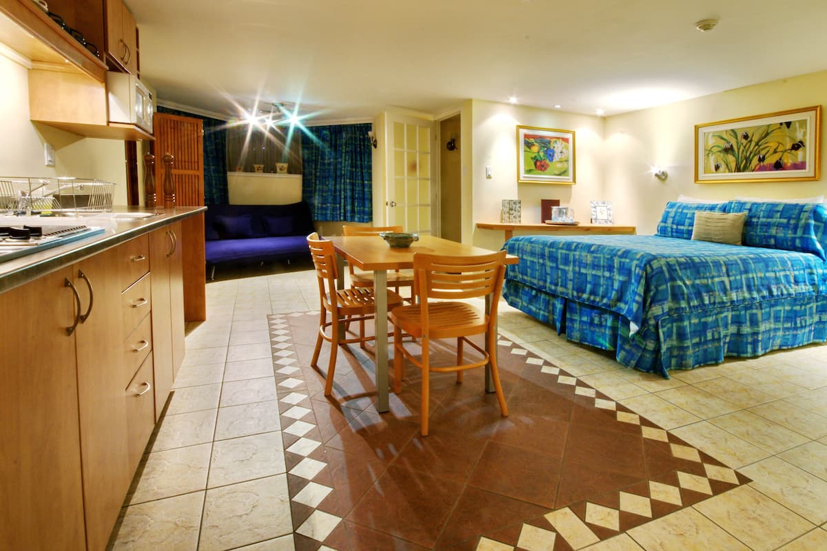 Quarto de hotel pequeno com cozinha, mesa de jantar, sofá e cama com colcha azul.