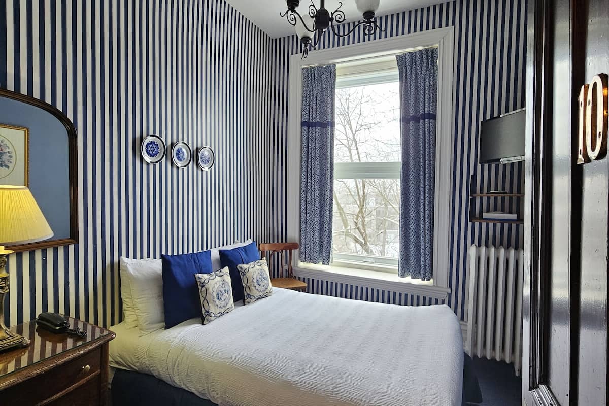 Quarto com uma cama grande, uma mesa de cabeceira, luminária, janela com cortinas e relógio na parede.