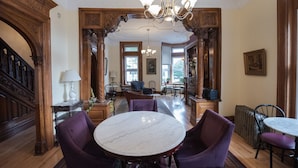 Um salão amplo com uma mesa de mármore, cadeiras roxas e um candelabro.
