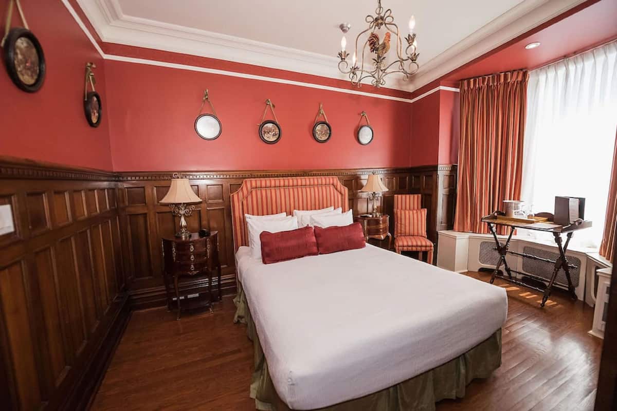 Quarto de hotel com uma cama grande, painéis de madeira, uma escrivaninha e uma cadeira.