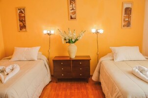 Quarto de hotel com duas camas, uma mesa de cabeceira com um vaso de flores e luminárias fixadas na parede.